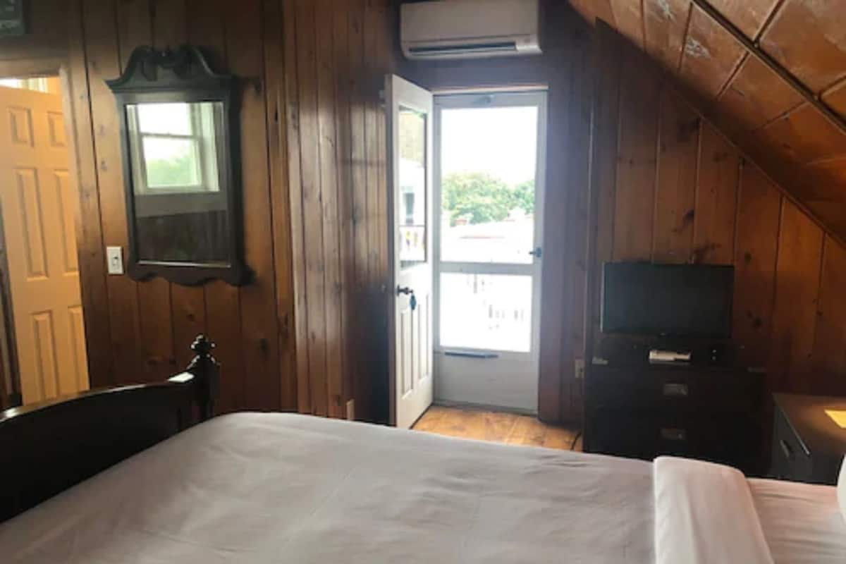 Quarto com cama, cómoda, televisão e porta para área externa.
