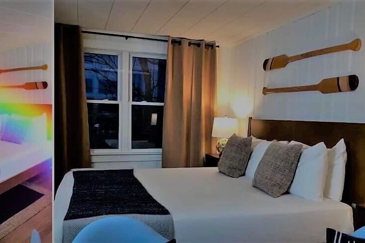 Quarto de hotel com uma cama, uma janela e um prancha de remo fixada na parede.