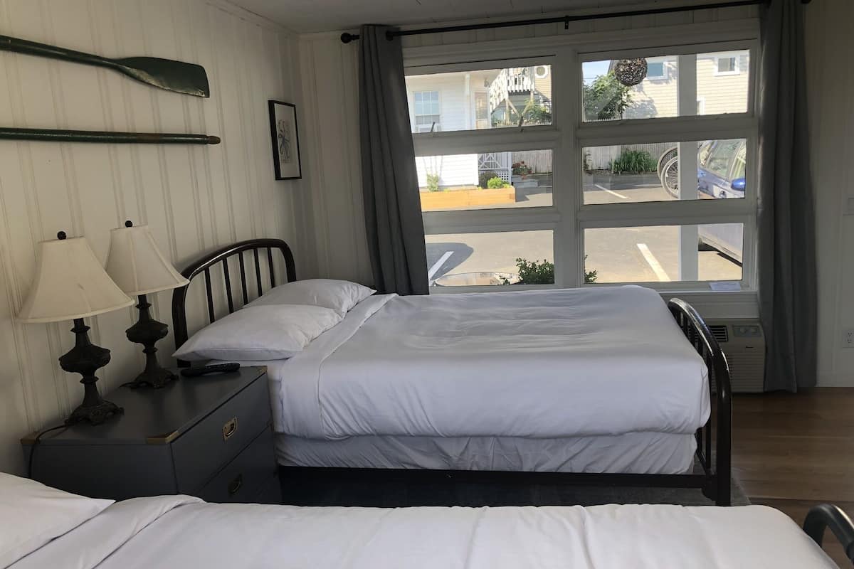 Quarto de hotel com cama, duas luminárias laterais, janela com cortinas e vista para a rua.