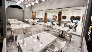 Um restaurante moderno com mesas e cadeiras brancas, piso estampado e teto com luminárias pendentes.
