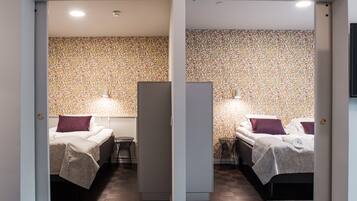 Quarto com duas camas, uma mesinha e um frigorífico.