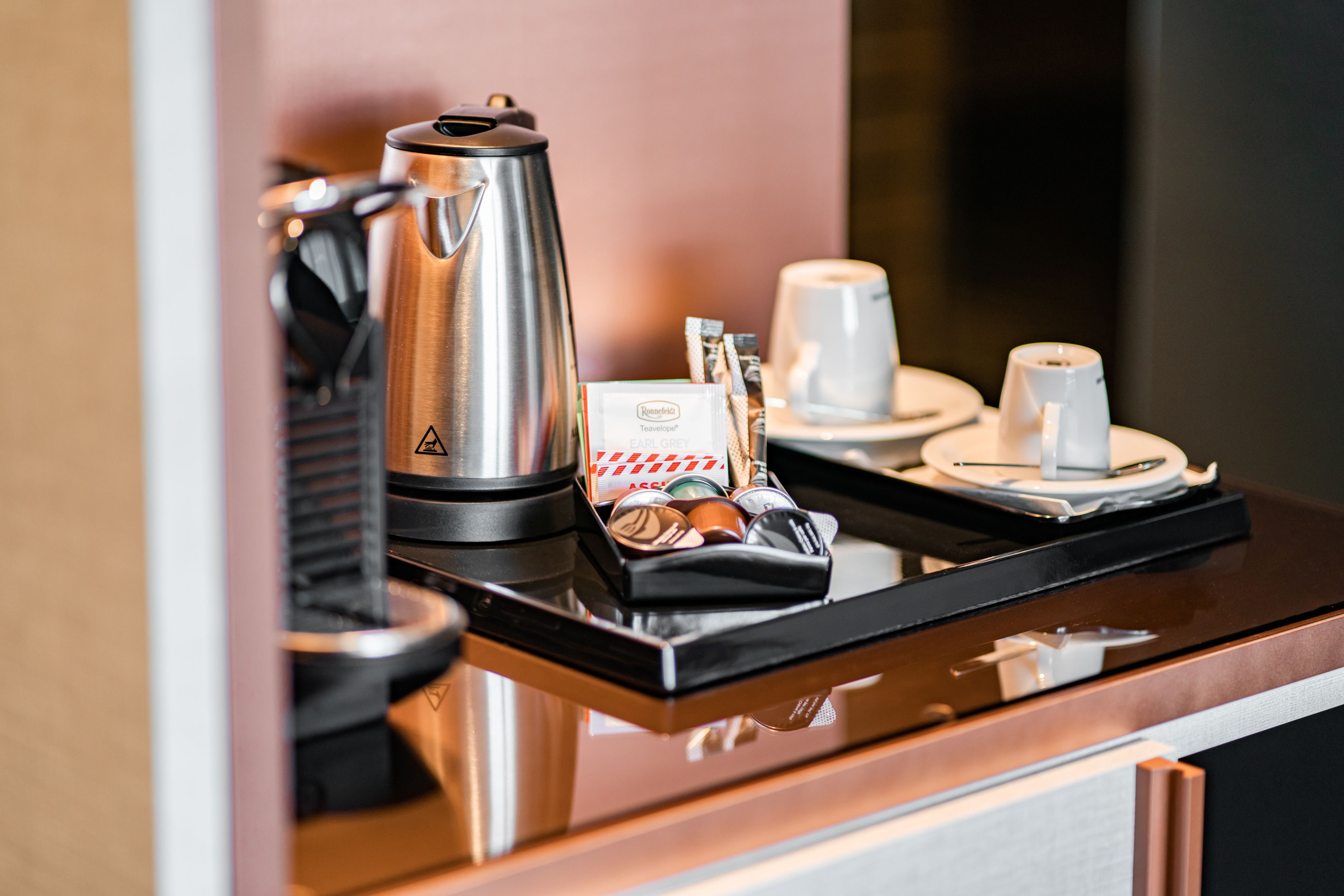 Uma estação de café com cafeteira, xícaras e um tabuleiro com cápsulas de café.