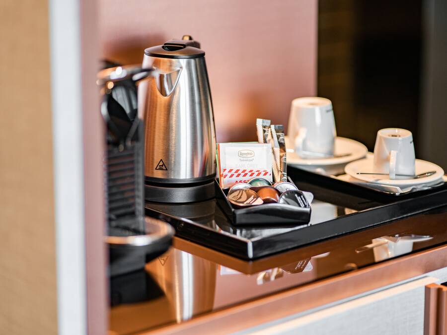 Uma estação de café com cafeteira, xícaras e um tabuleiro com cápsulas de café.
