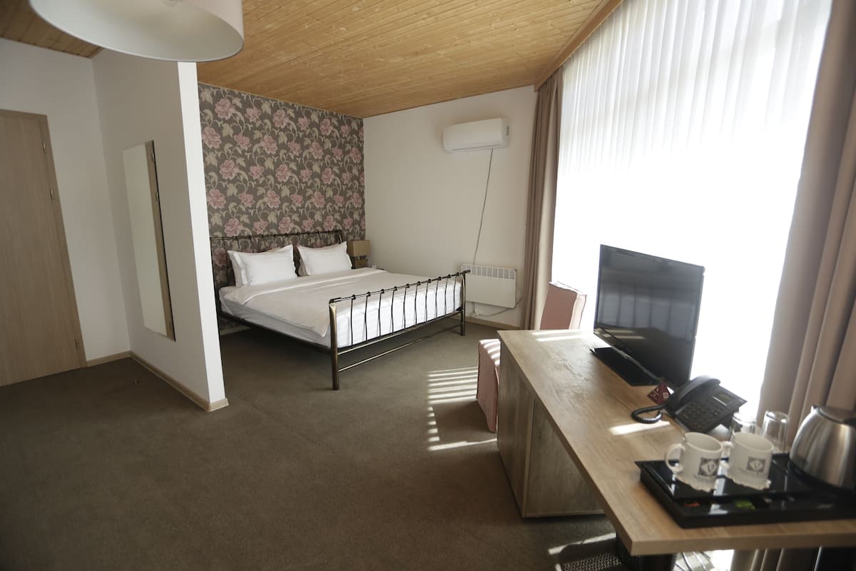 Quarto de hotel com cama, escrivaninha com computador, televisão e bandeja para café.