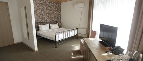 Quarto de hotel com cama, escrivaninha com computador, televisão e bandeja para café.