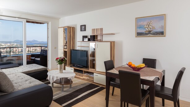 Sala moderna com televisão, mesa de jantar e cadeiras. Possui uma varanda com vista para a cidade e montanhas.