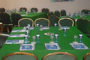 Sala de conferência com mesas verdes, cadeiras, garrafas de água e placas de identificação.
