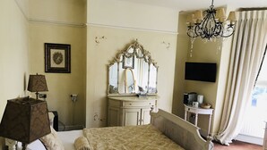 Um quarto com uma cama, uma penteadeira com espelho, um lustre, uma televisão e uma janela com cortinas.