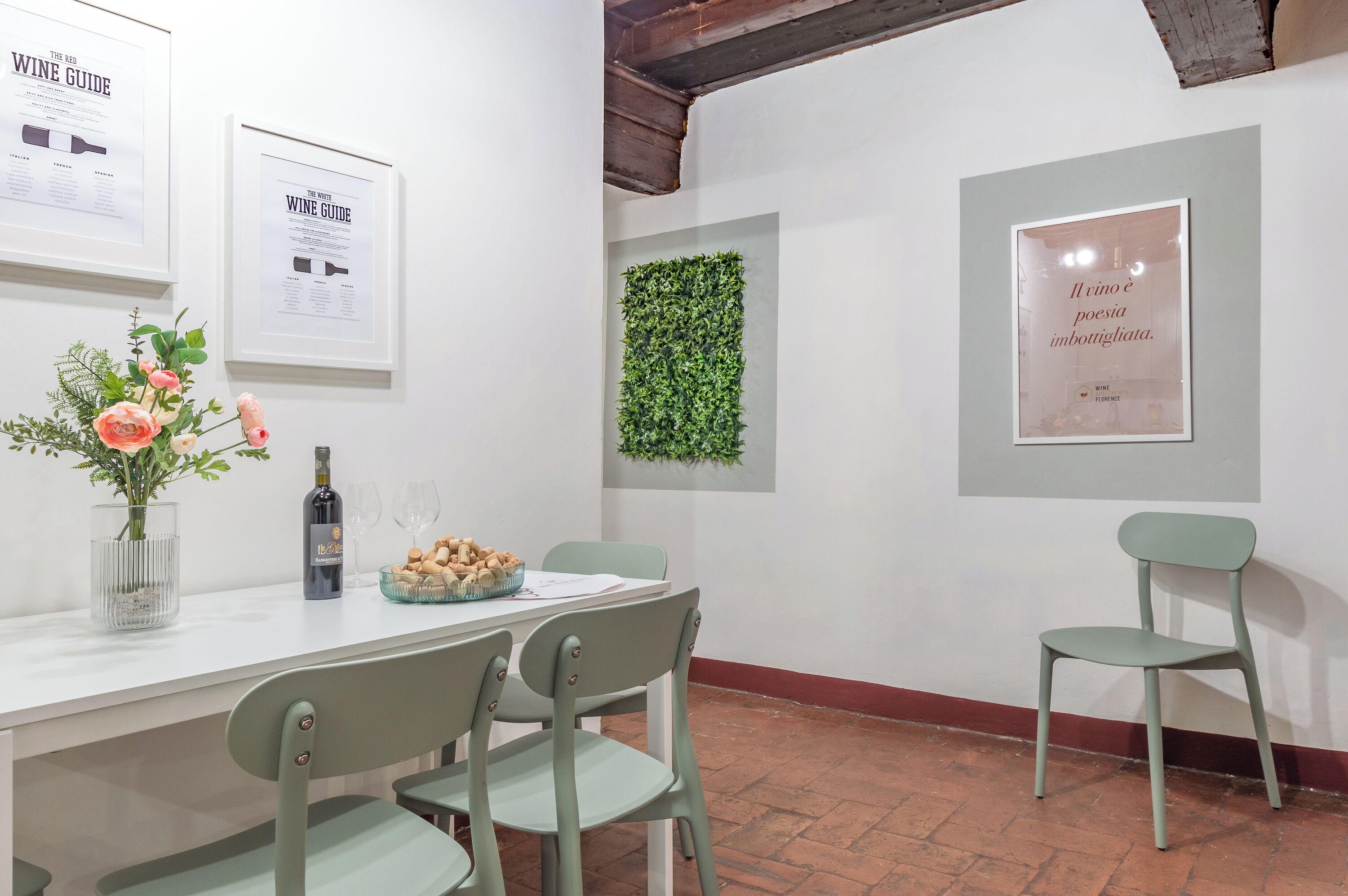 Uma área de refeições com uma mesa branca, duas cadeiras verdes, uma garrafa de vinho e um recipiente com rolhas de vinho.