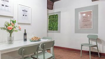 Uma área de refeições com uma mesa branca, duas cadeiras verdes, uma garrafa de vinho e um recipiente com rolhas de vinho.