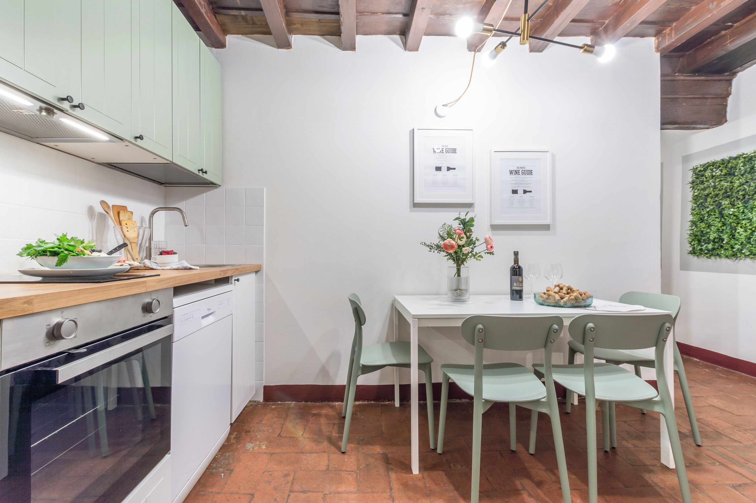 Uma cozinha moderna com área de jantar, com bancada branca, forno embutido e mesa com cadeiras.