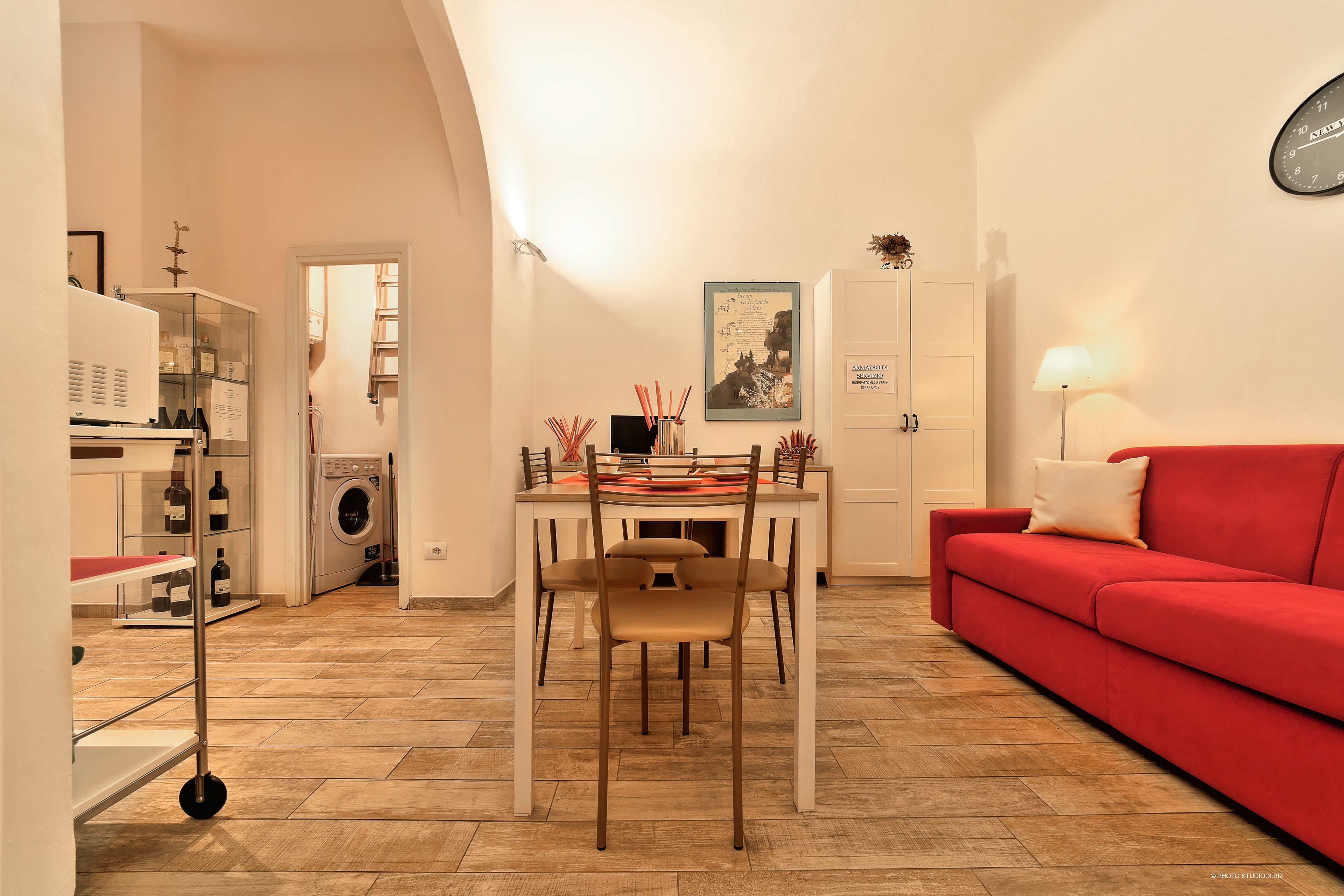 Um espaço habitacional compacto com área de refeições, um sofá vermelho, uma máquina de lavar e um pequeno espaço cozinha.