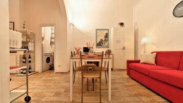 Um espaço habitacional compacto com área de refeições, um sofá vermelho, uma máquina de lavar e um pequeno espaço cozinha.