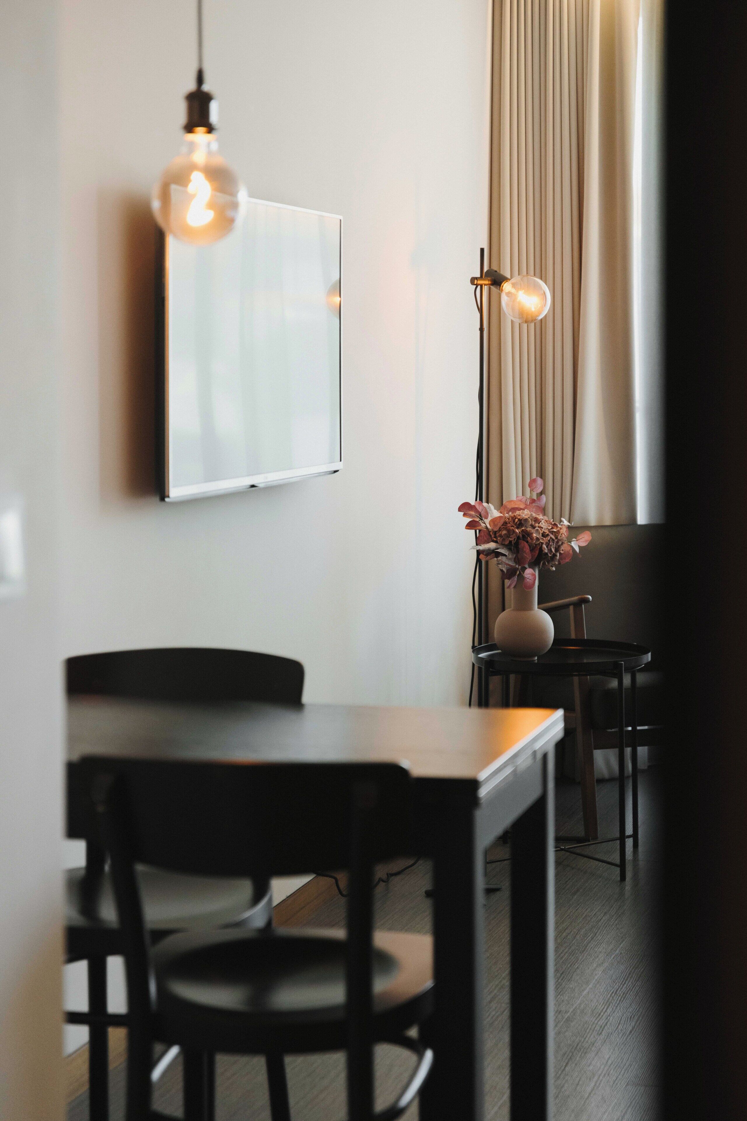Uma sala de jantar moderna com mesa, cadeiras, um vaso com flores e luminárias pendentes.