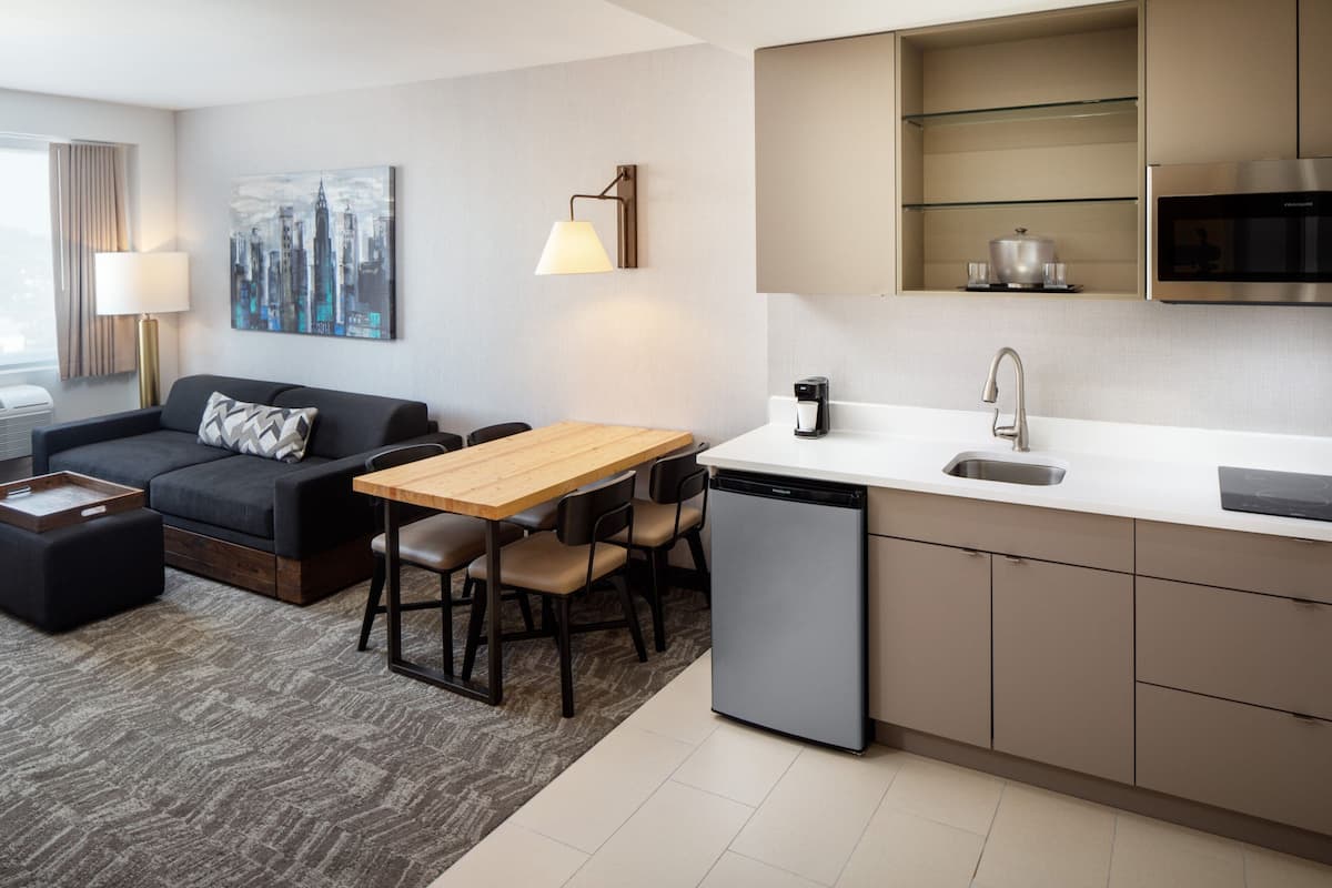 Quarto de hotel moderno com área de estar, cozinha compacta e mesa de jantar.