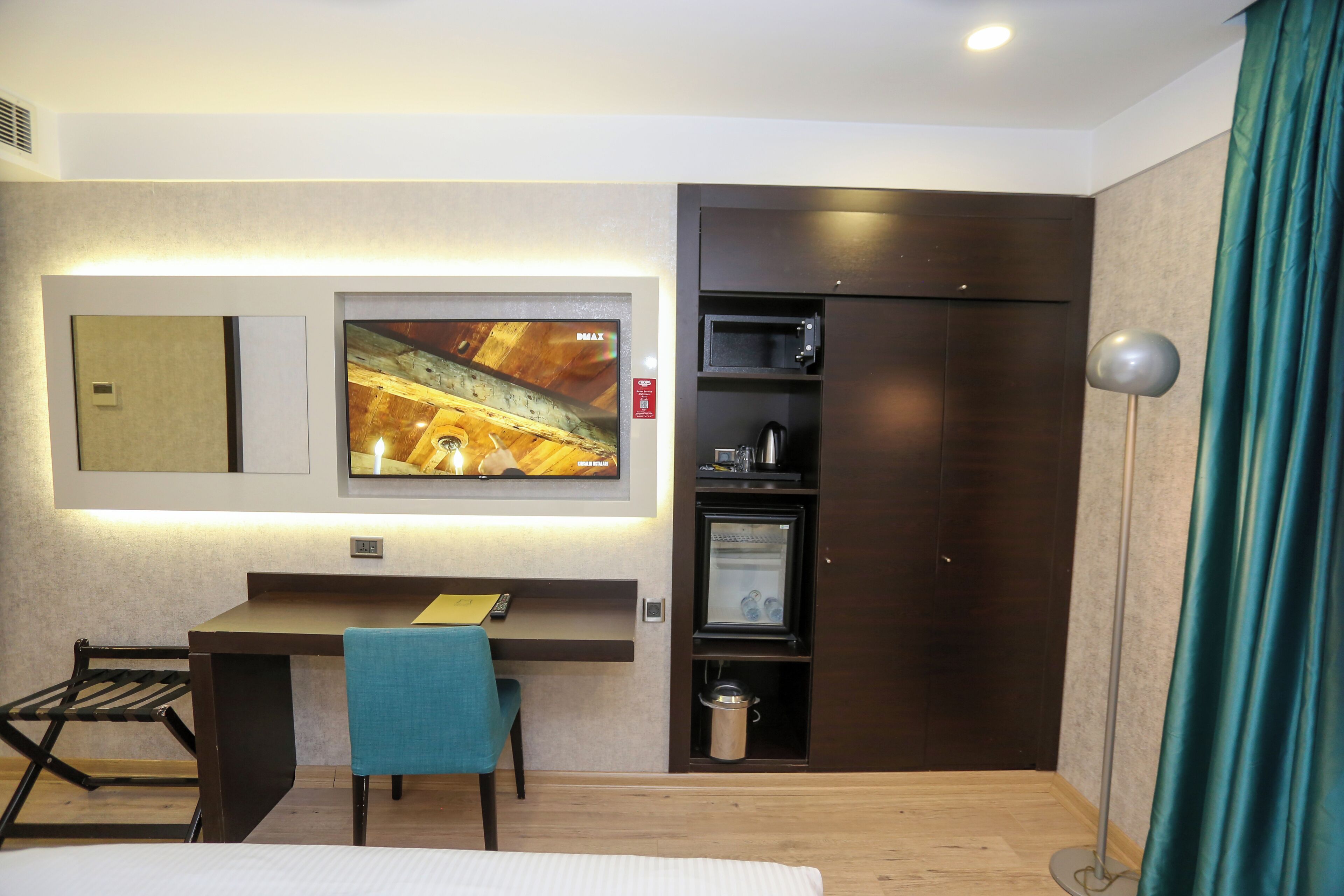 Quarto de hotel com uma cama, escrivaninha, cadeira, televisão, micro-ondas e guarda-roupa.