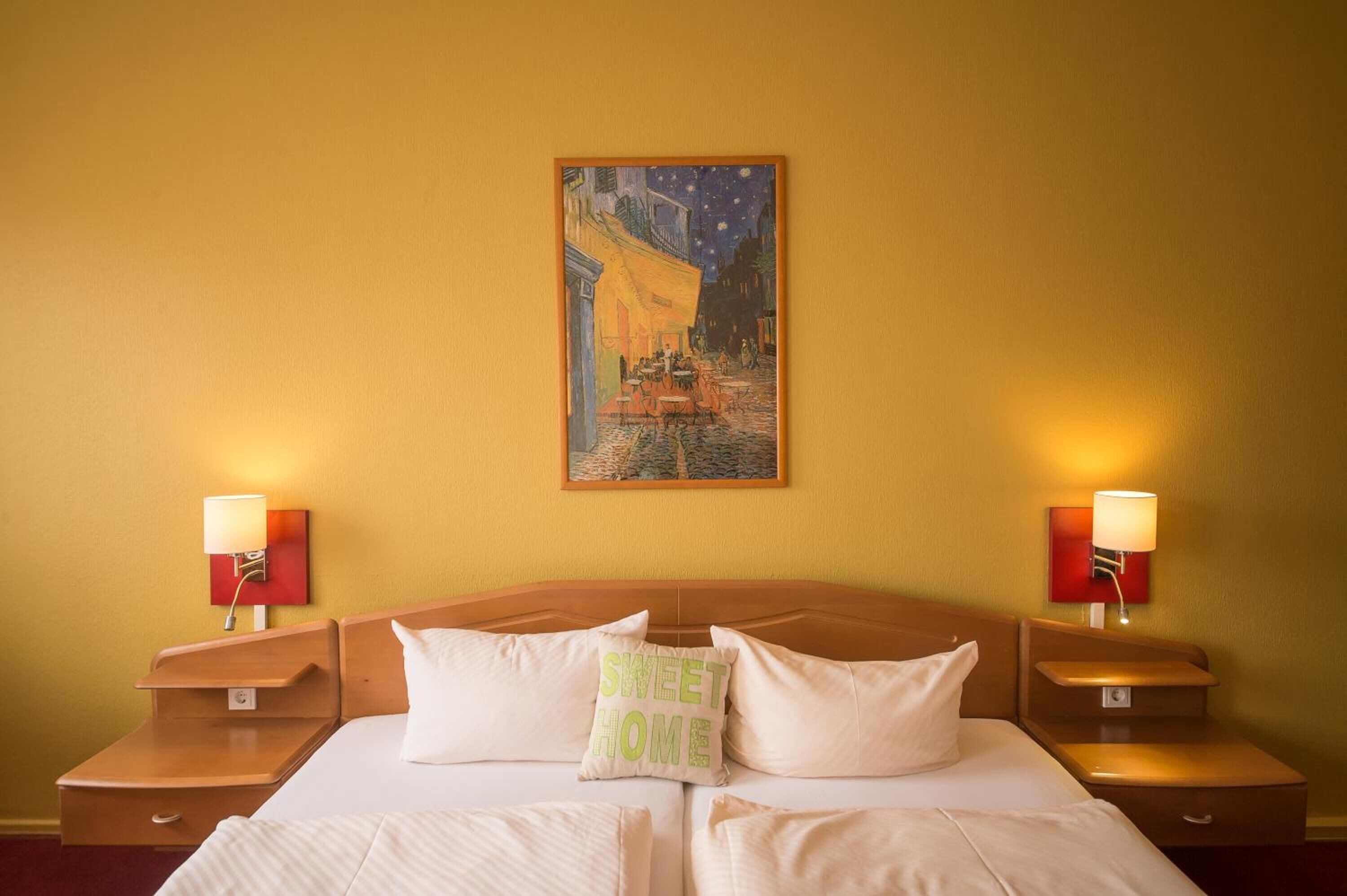 Quarto de hotel com uma cama, duas mesas de cabeceira, um criado-mudo, um quadro na parede e duas luminárias.