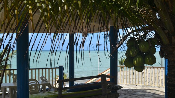Um espaço de descanso à beira-mar, com rede, espreguiçadeiras e vista para o oceano.