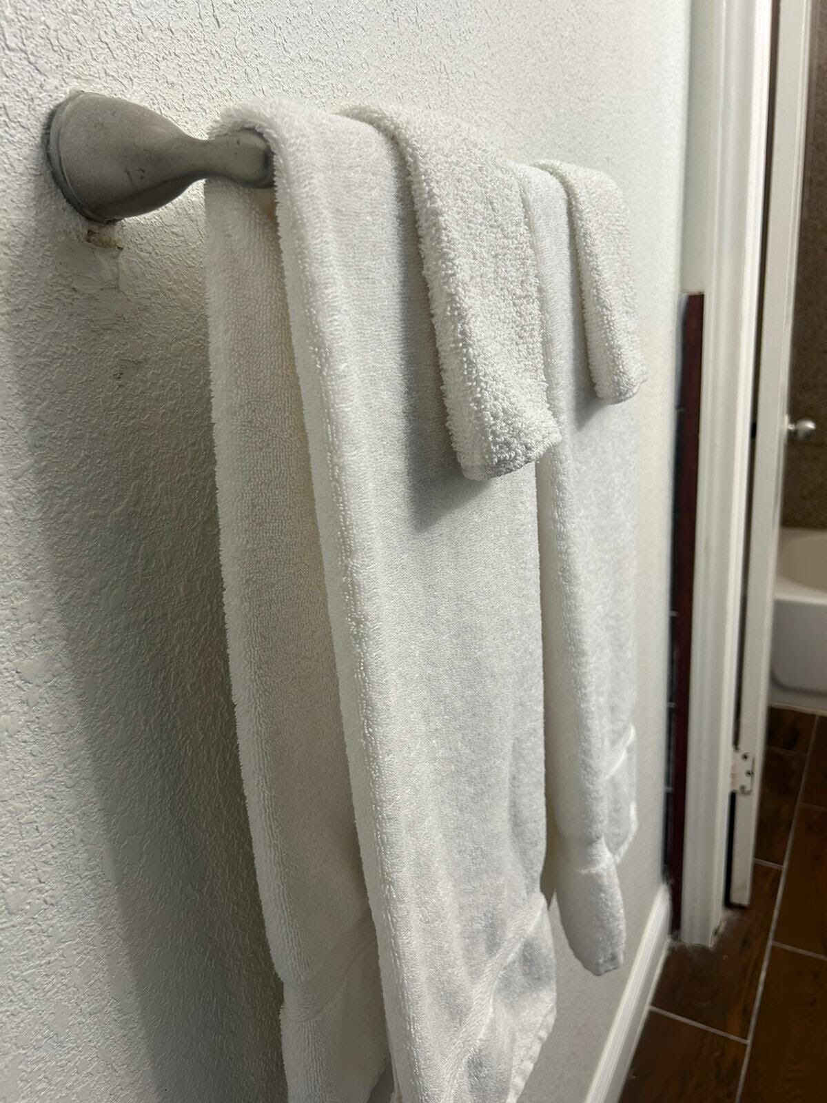 Uma toalha branca pendurada em um porta-toalhas fixado na parede de um banheiro.