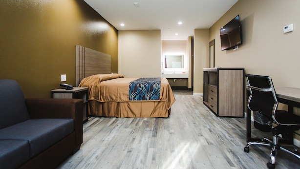 Quarto de hotel com cama, escrivaninha, cadeira, televisão e armário.