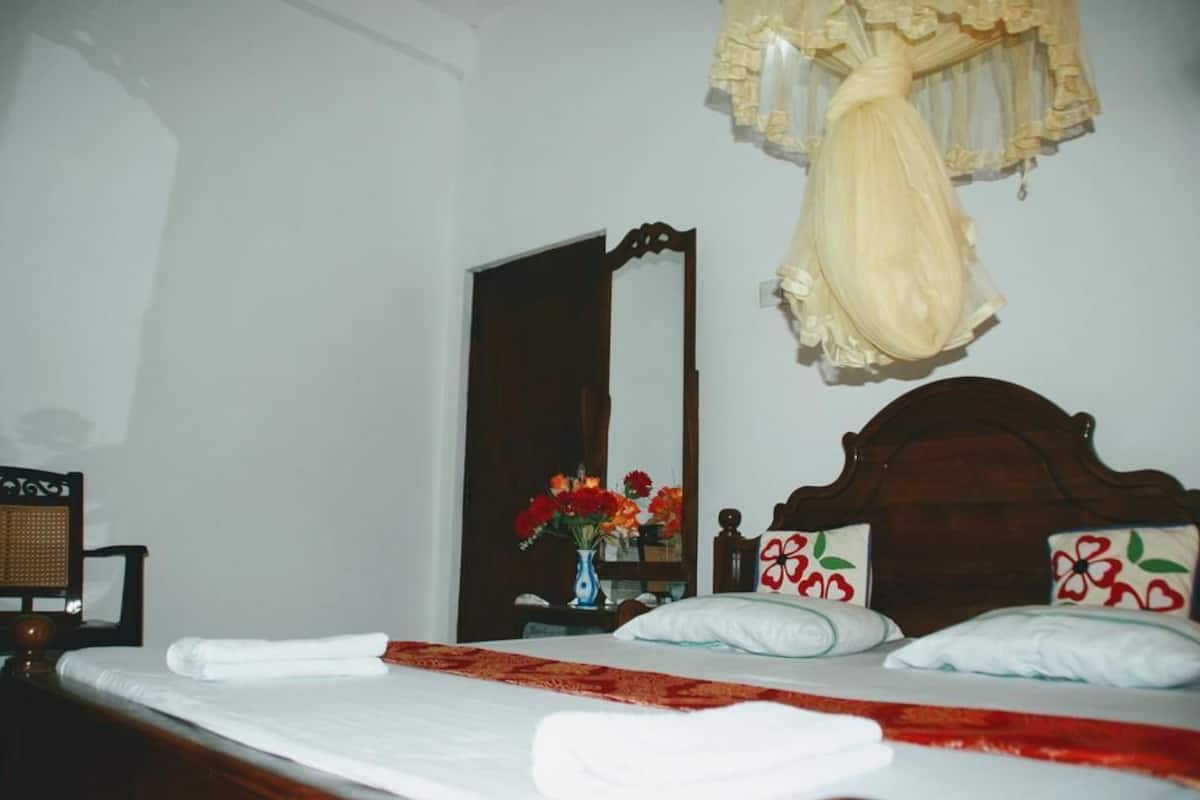 Cama bem arrumada com lençóis brancos, cabeceira de madeira e almofadas decorativas com estampas florais.