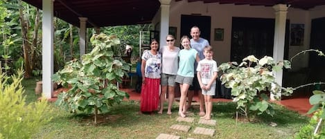 Uma área externa coberta com telhado vermelho, colunas brancas e um caminho pavimentado.