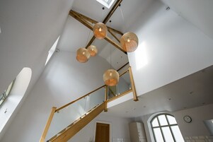 Interior moderno com escadaria de madeira, claraboia e uma grande janela em arco.