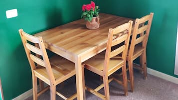Uma área de refeições com uma mesa de madeira e quatro cadeiras, uma televisão fixada na parede e duas molduras com imagens.