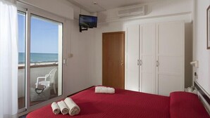 Quarto de hotel com cama, televisão, guarda-roupa e varanda com vista para o mar.