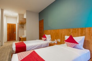Quarto de hotel com duas camas, cabeceira de madeira, uma mesinha de cabeceira, um telefone e um cabideiro.
