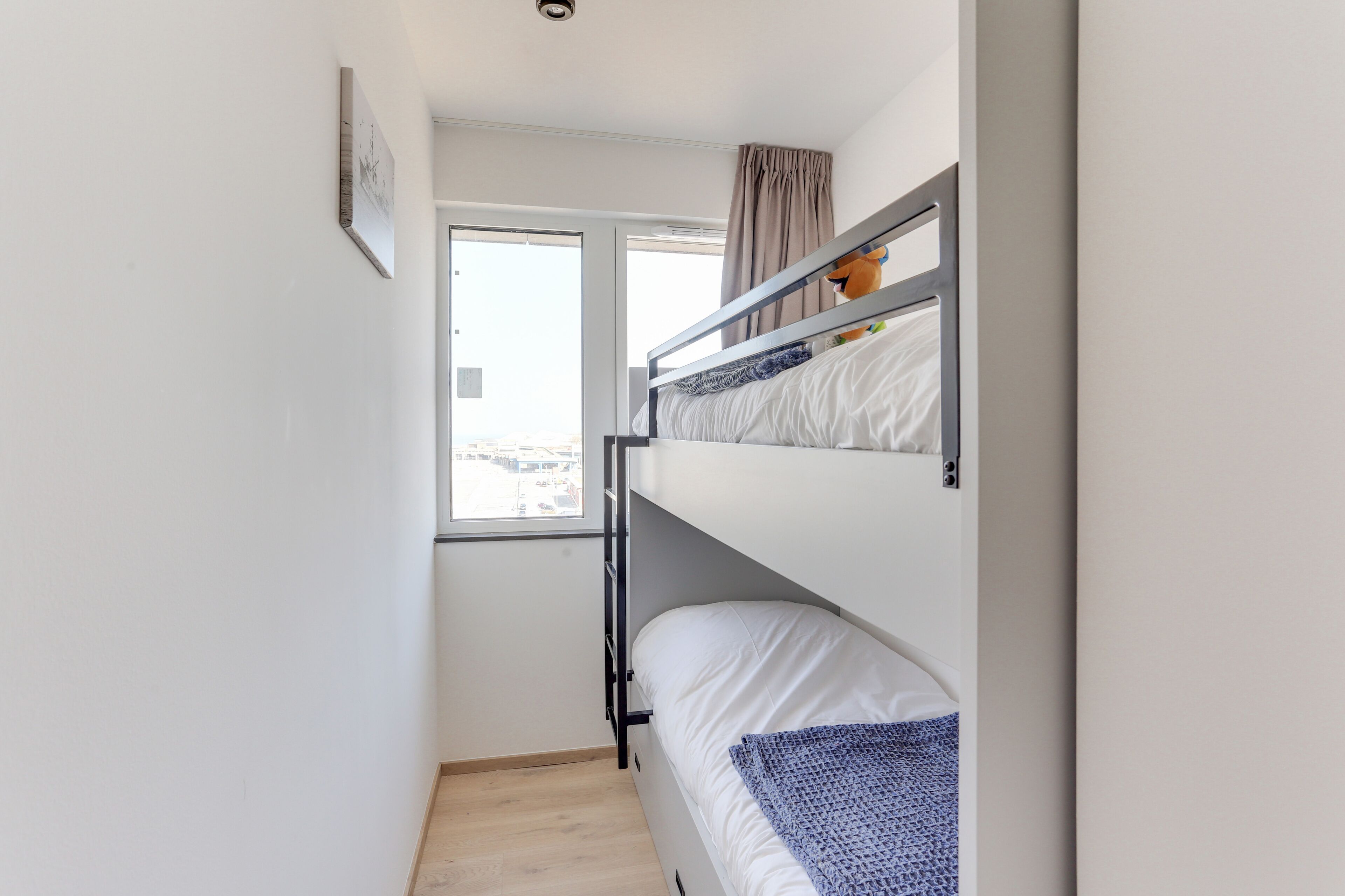 Quarto pequeno e compacto com beliches, uma janela e uma porta.