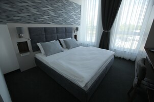 Quarto de hotel moderno com uma cama grande, cabeceira com padrão geométrico, mesa de cabeceira e uma cadeira.