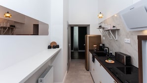 Uma cozinha moderna com bancadas brancas, fogão preto e geladeira de aço inoxidável. Duas luminárias pendentes iluminam o espaço acima das bancadas.
