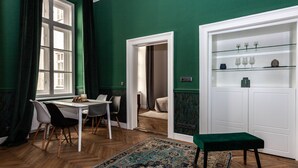 Um quarto com uma mesa de jantar, cadeiras, um banco verde, um tapete estampado e uma vitrine de vidro com objetos.