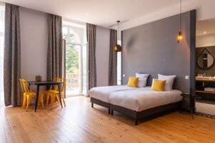 Quarto de hotel moderno com uma cama grande, uma mesa pequena, cadeiras amarelas e vista para o exterior.