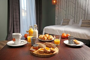 Mesa de café da manhã com croissants, torradas, suco de laranja e uma xícara de café.
