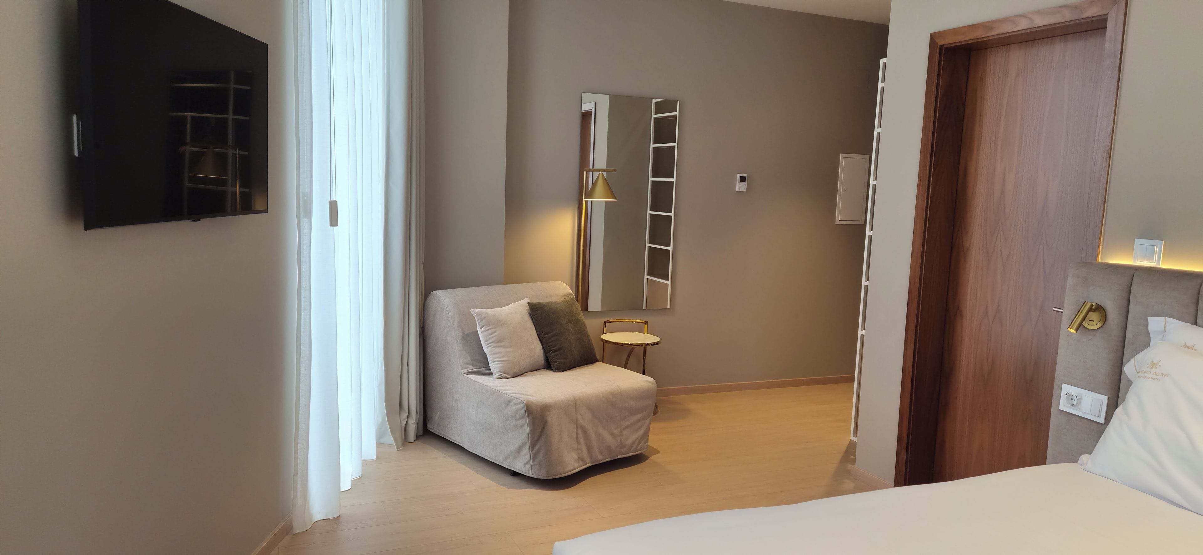 Quarto de hotel com cama, sofá, mesa pequena, cadeira, televisão e porta.