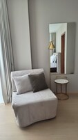 Quarto moderno com sofá-cama, uma mesinha redonda, abajur e um espelho grande.