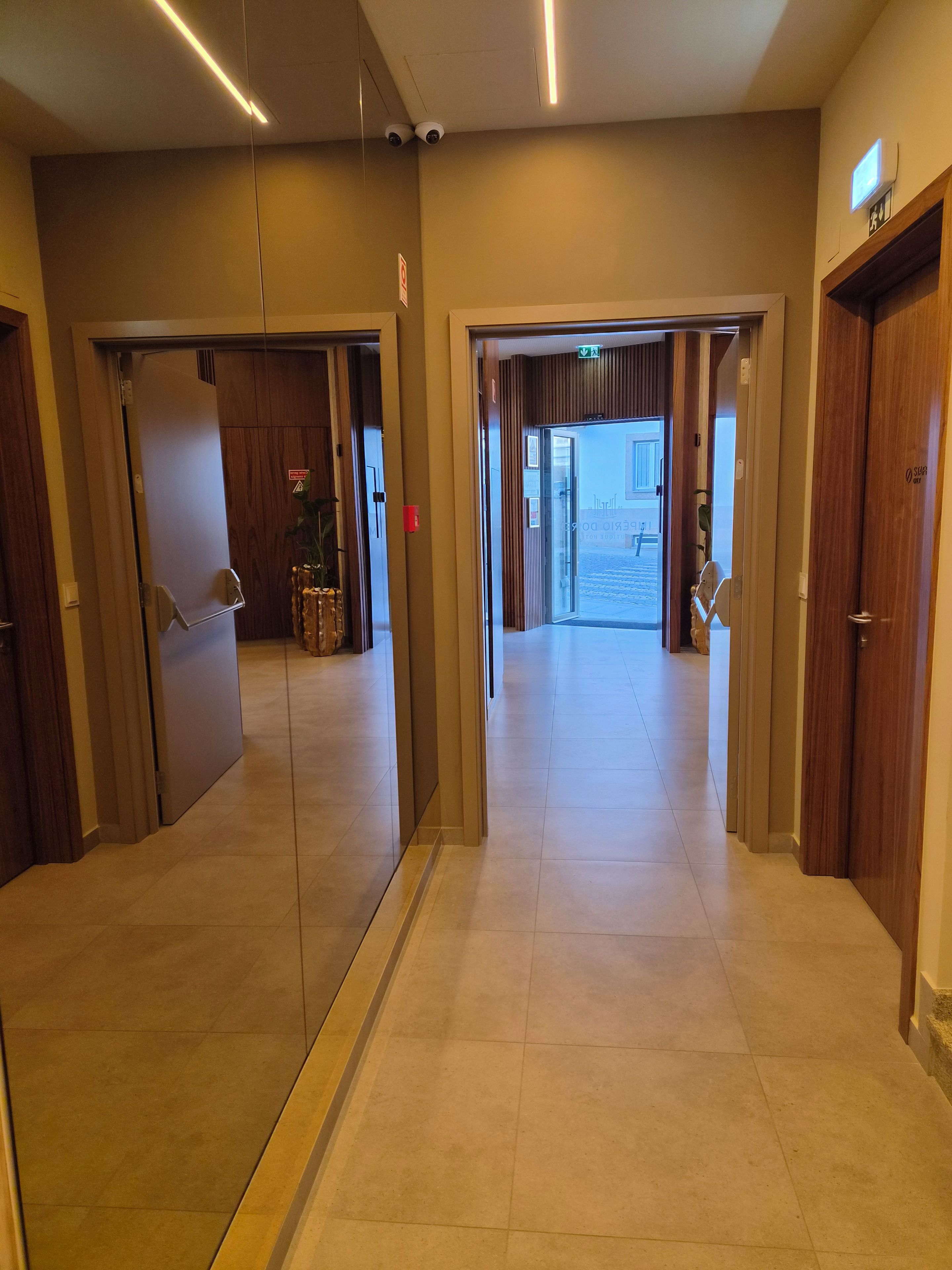 Corredor de hotel com design moderno, apresentando uma porta de vidro, uma planta e placa indicando área para fumantes.