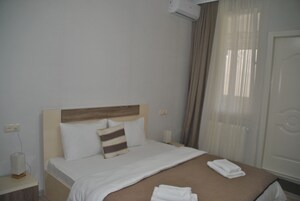 Quarto de hotel com cama, mesa de cabeceira, ar condicionado, janela com cortinas e porta.