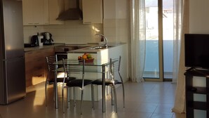 Uma cozinha moderna com ilha central, eletrodomésticos de aço inoxidável e uma área de refeições com mesa e cadeiras de vidro.