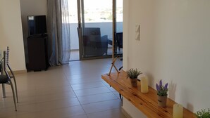 Quarto amplo com um banco de madeira, uma TV e uma porta de vidro deslizante que dá para uma área externa.
