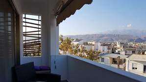 Uma varanda com mobiliário de vime, vista para um horizonte urbano e montanhas ao longe.