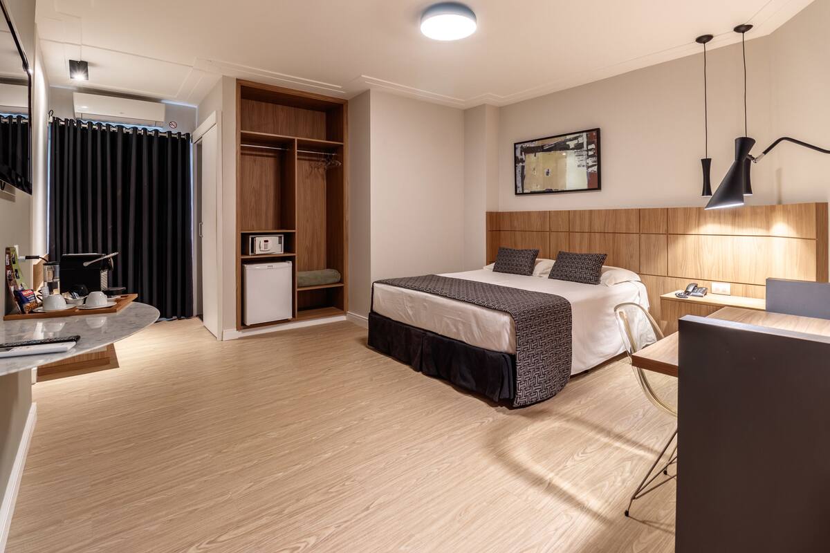 Quarto de hotel moderno com uma cama grande, uma escrivaninha, um guarda-roupa e uma área de chuveiro.