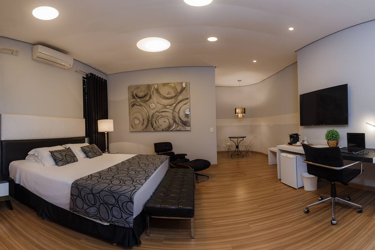 Quarto de hotel moderno com uma cama grande, uma escrivaninha, uma cadeira, uma TV e ar condicionado.