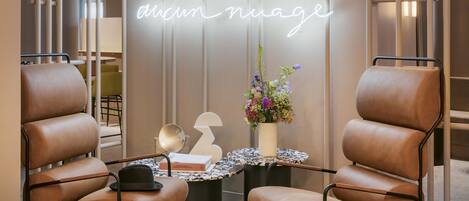 Uma área de estar moderna com poltronas de couro, uma mesa redonda com um vaso de flores e um letreiro de neon na parede.