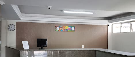 Uma área de recepção com balcão de mármore, um relógio e uma obra de arte colorida na parede.