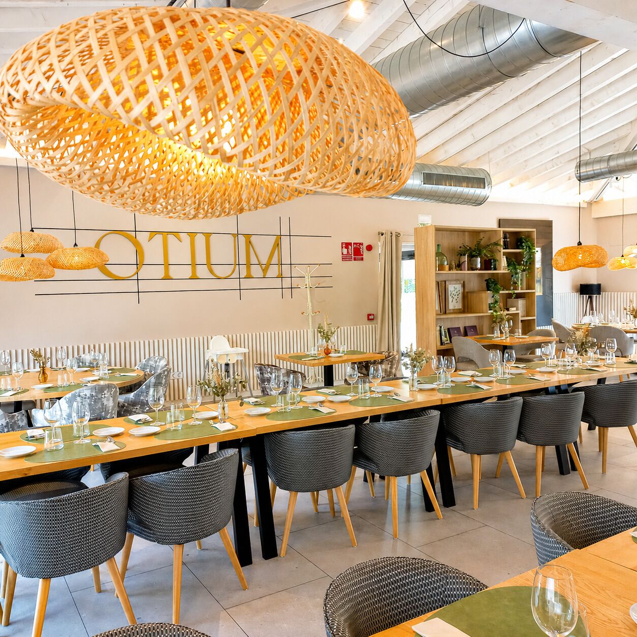 Interior de restaurante com uma mesa de jantar comprida, várias cadeiras e um grande candeeiro de fibra natural.