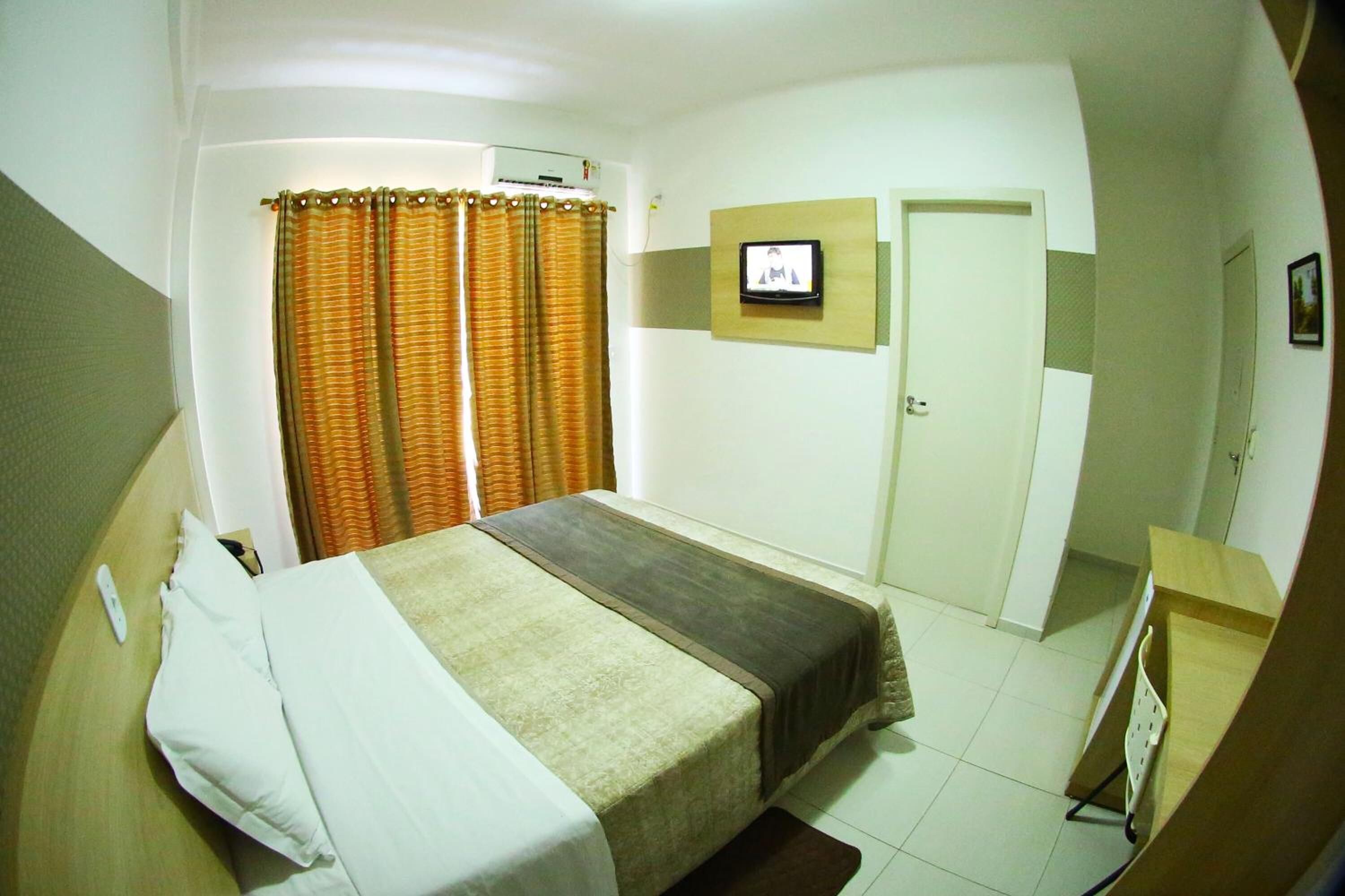 Quarto de hotel com cama, televisão na parede e porta que dá para outro aposento.
