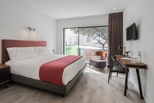 Quarto de hotel moderno com uma cama grande, uma escrivaninha e uma televisão.